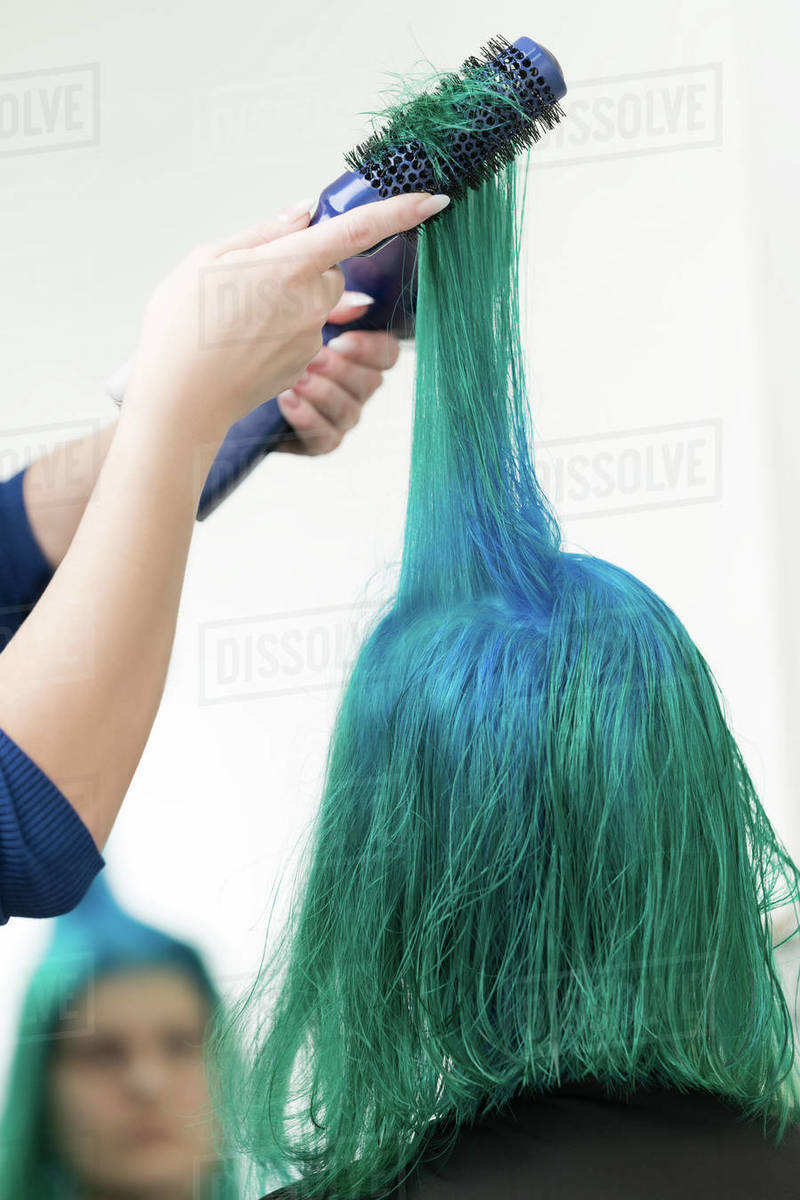 Hairdresser combs and dries hair of emerald color with hairdryer after ...