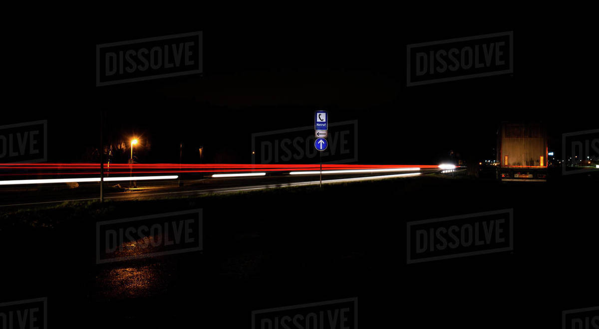 Cars passing an emergency stop sign at night on a busy highway ...