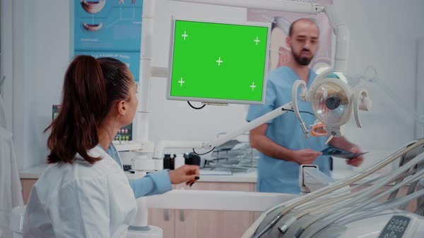 Dentist looking at monitor with horizontal green screen for oral care ...