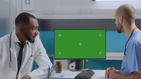 Multi-ethnic team looking at mock up green screen chroma key computer ...
