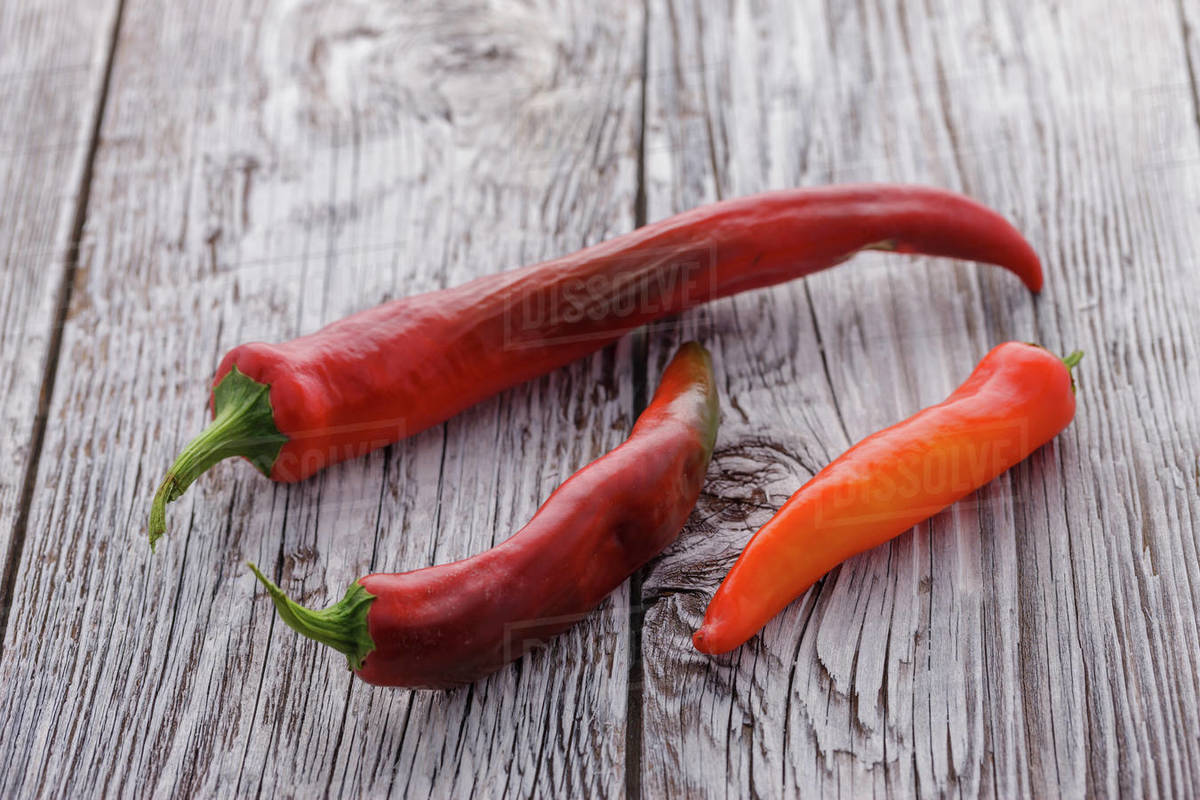 A close up of three red spicy peppers on a wood background. - Royalty ...