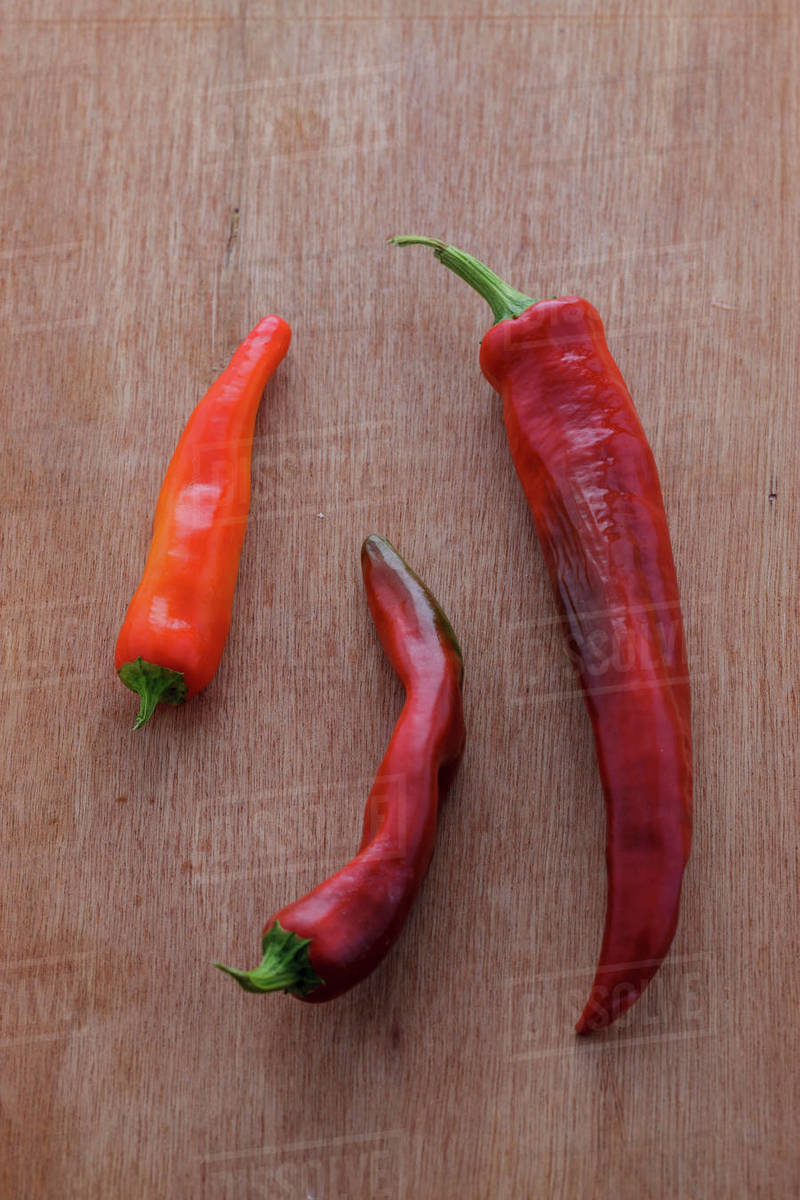 A close up of three red spicy peppers on a wood background. - Stock ...