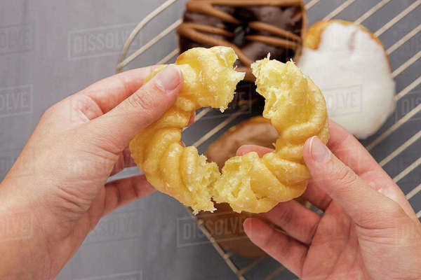 Pulling apart a glazed doughnut above a rack of assorted doughnuts ...