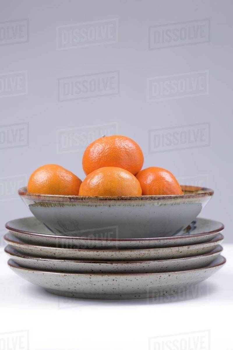 A studio photo of small oranges in a bowl on top of stacked plates ...