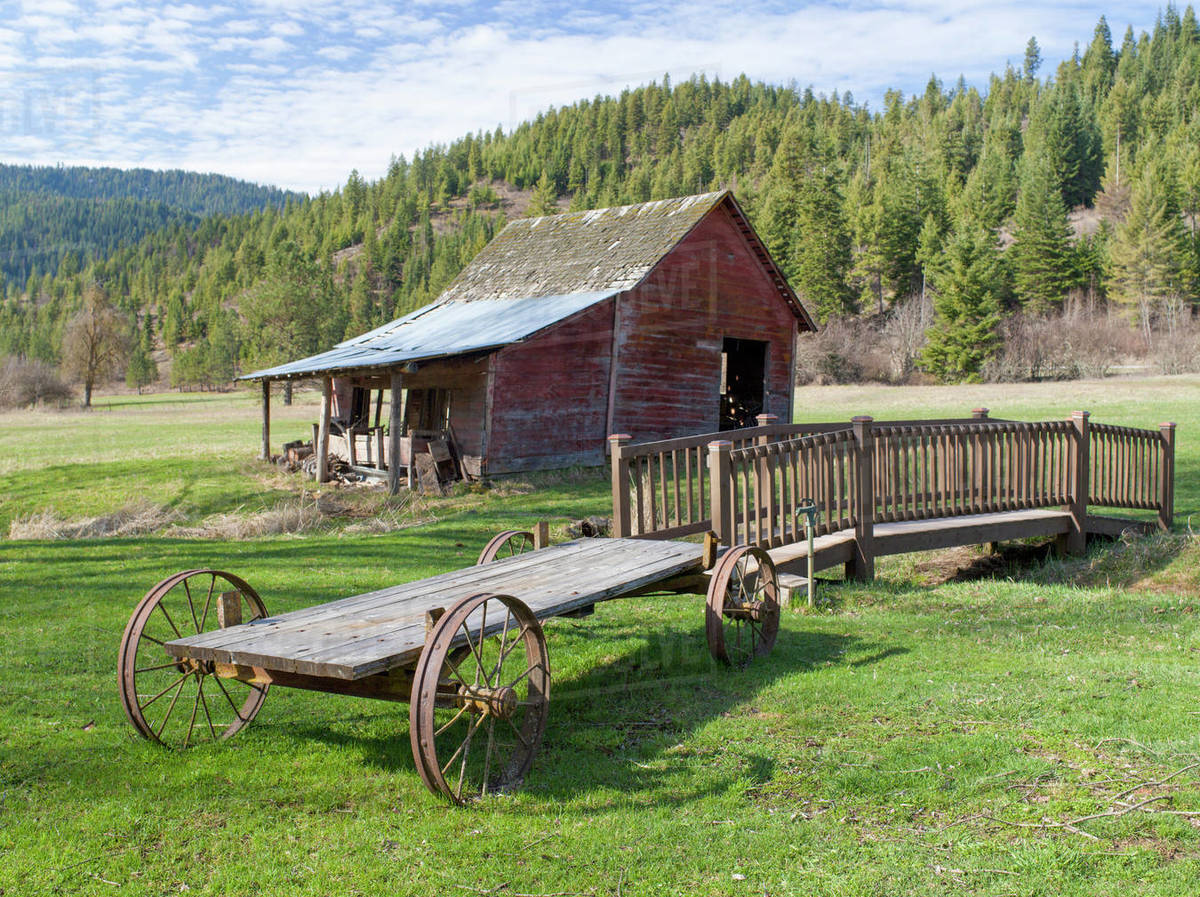 An old wagon sits near a small bridge and a small barn in north Idaho ...