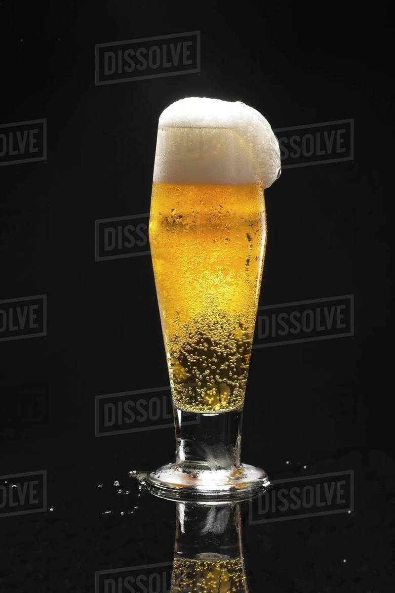 A close up uof a glass of beer against a black background starting to ...