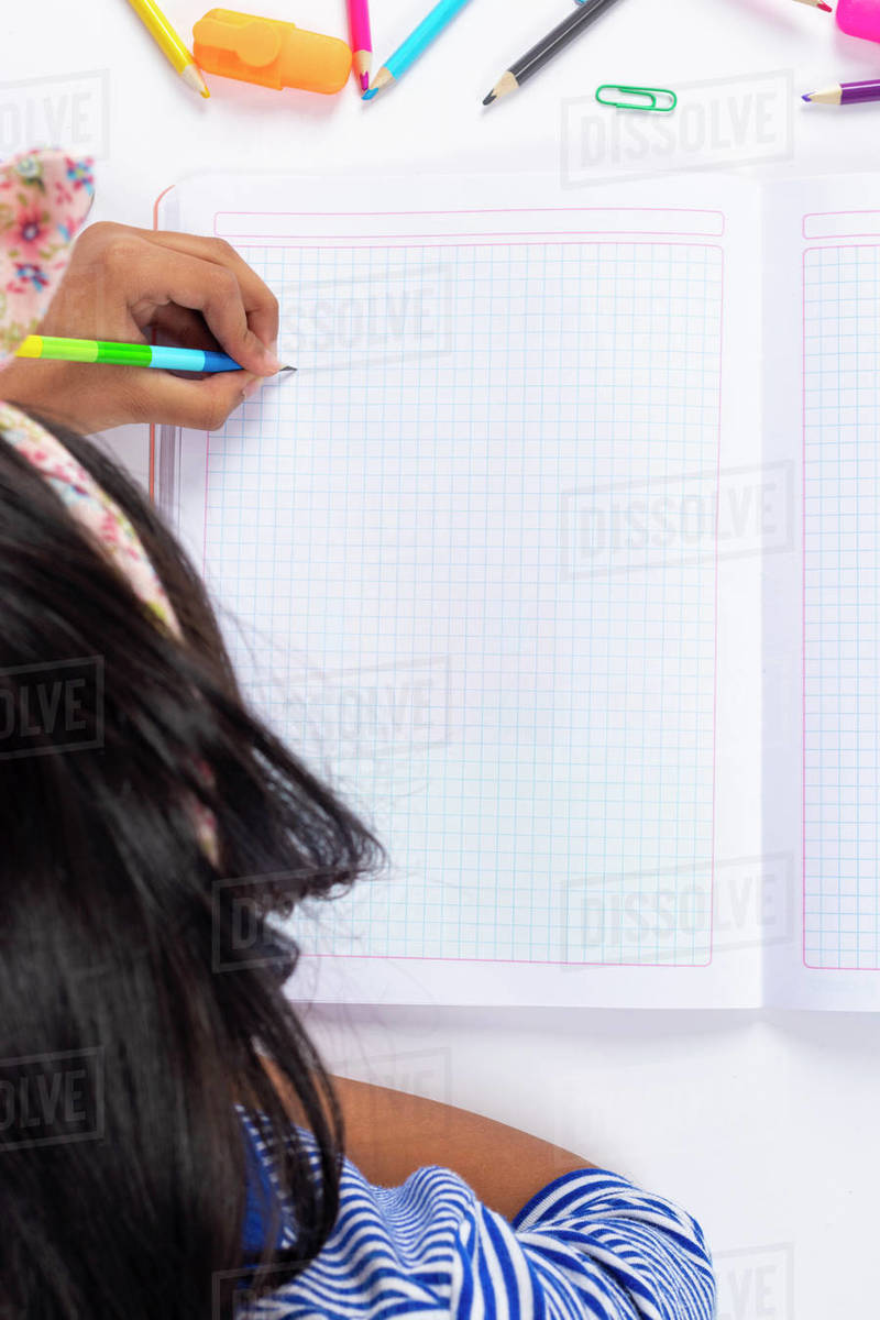 Cute left-handed girl is writing with a pencil in her notebook ...