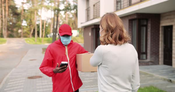 Close up of delivery man in mask and red cap delivering order home and ...