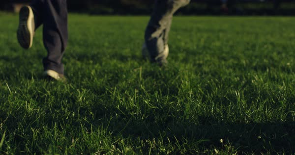 Close up of the feet of boys running on the green grass of the field ...
