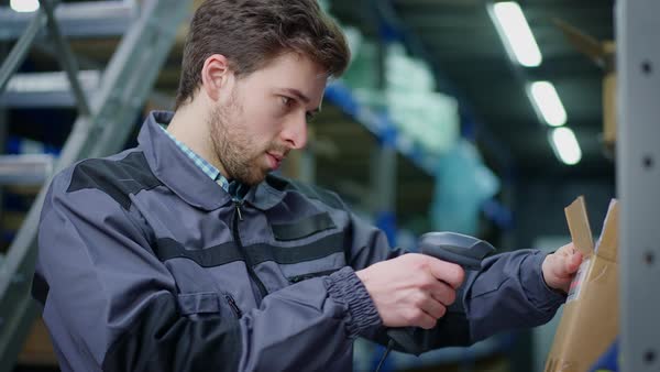 Brunette man scanning barcode on cardboard box with scanner in urban ...
