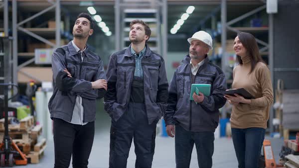 Group of people standing in warehouse looking up at stock racks talking ...
