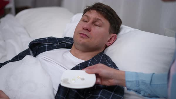 Desperate depressed ill man lying in bed as unrecognizable woman ...