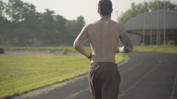 Back view of sportive Caucasian man jogging on stadium in summer ...