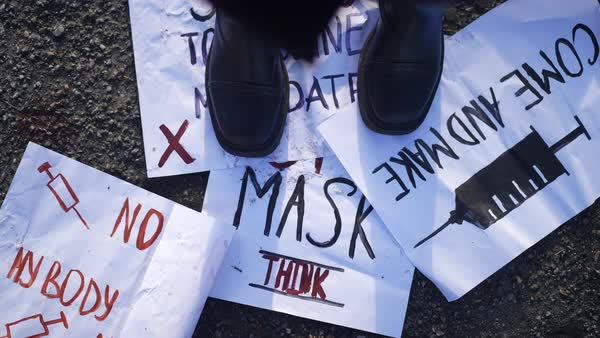 Feet stomping on anti-vax placards on the ground. Unrecognizable ...