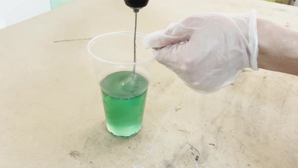 Gloved hands stir the green caustic liquid of green color in a plastic ...
