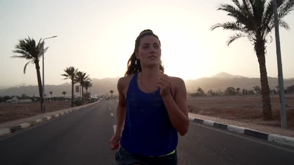 Portrait of caucasian girl jogging at tropical highway at sunrise slow ...