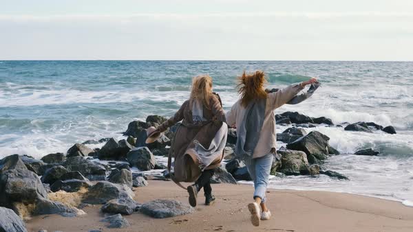 Woman couple run holding hands along the sea beach. Two girls running ...
