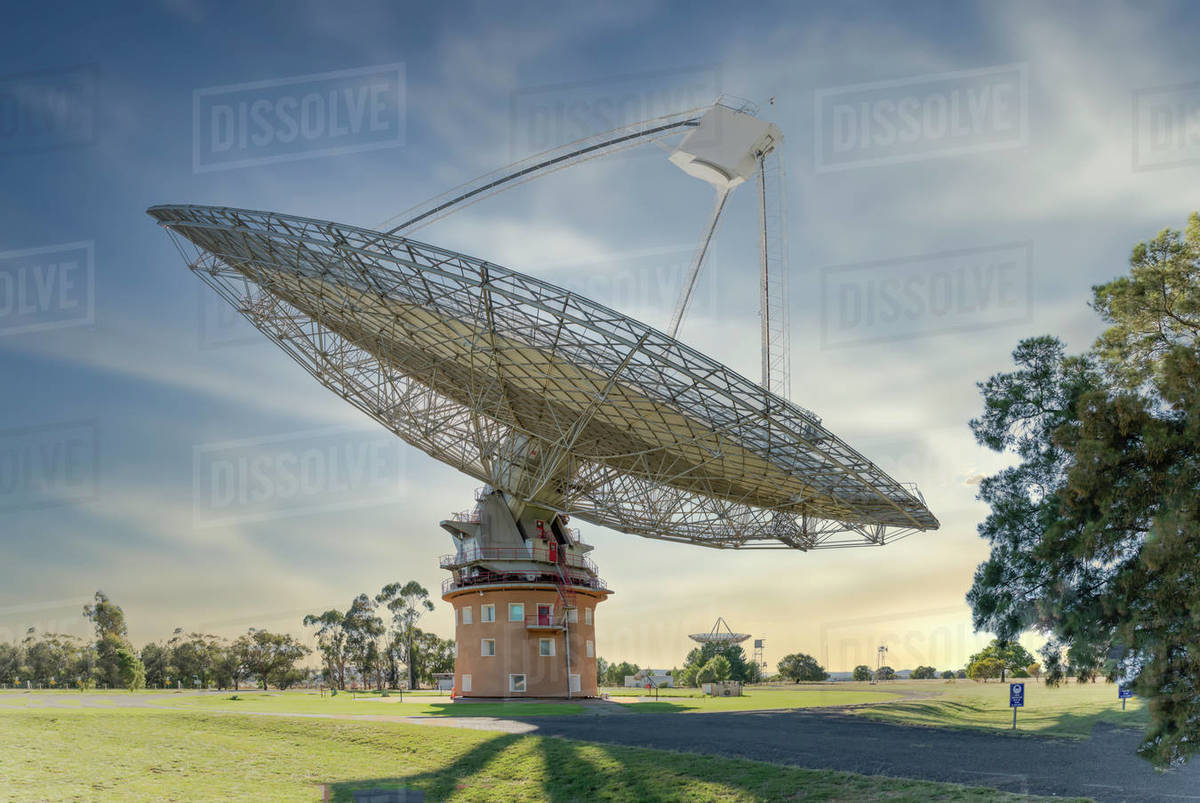 A large outdoor scientific radio telescope in the sunshine in a green ...