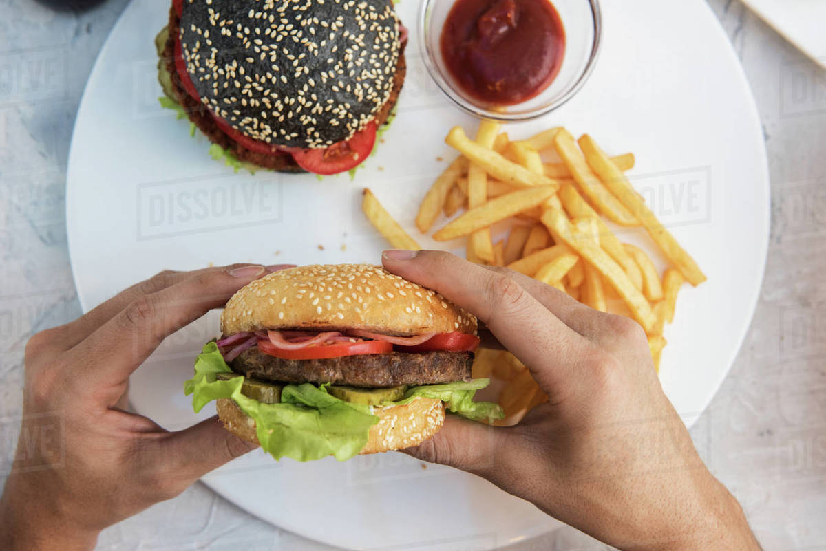 Man eating burgers at table, pov view - Stock Photo - Dissolve