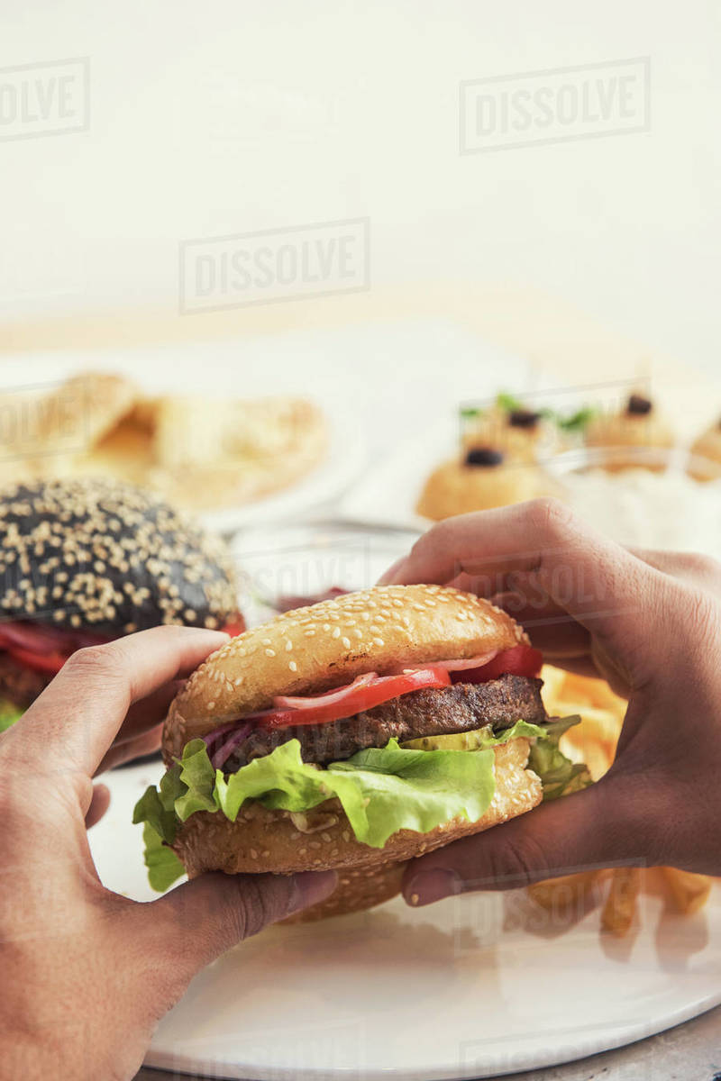 Man eating burgers at table, pov view - Royalty-free Stock Photo | Dissolve
