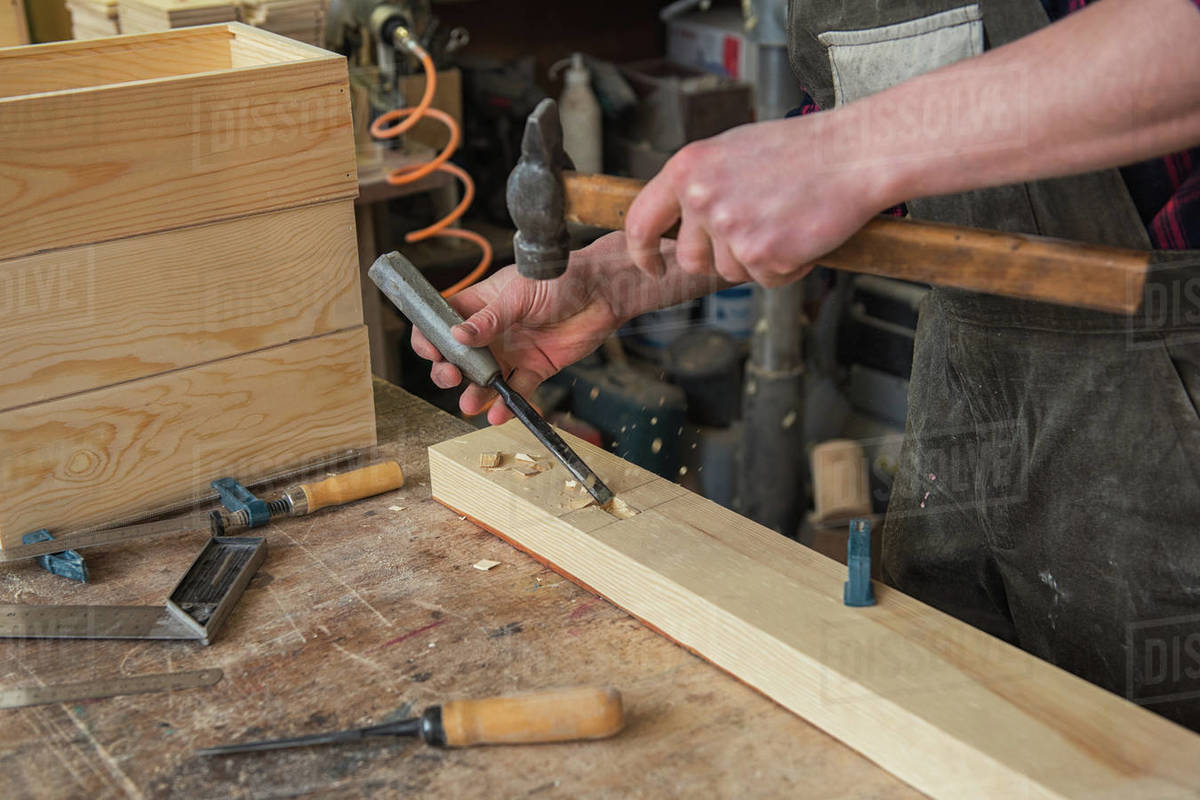Carpenter working with a chisel and hammer in a wooden workshop ...