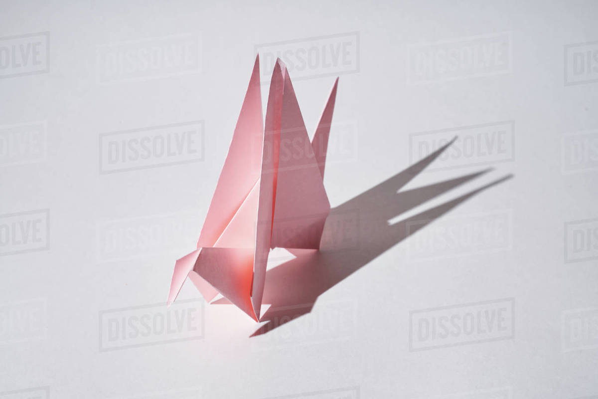 Pink paper dragon figurine stands on a white background in hard light ...