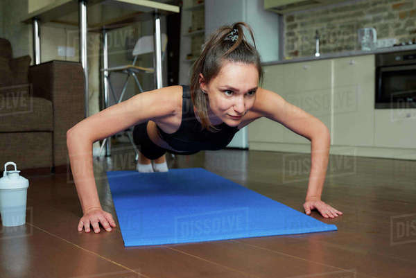 A sporty skinny girl in a black workout tight suit is doing push-ups to ...
