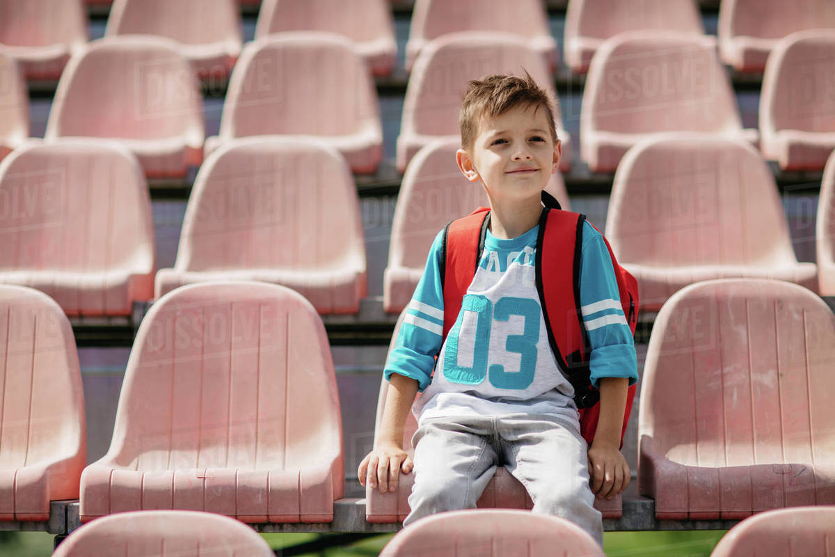 Portrait of a happy school boy sitting on a seat and watching a game ...