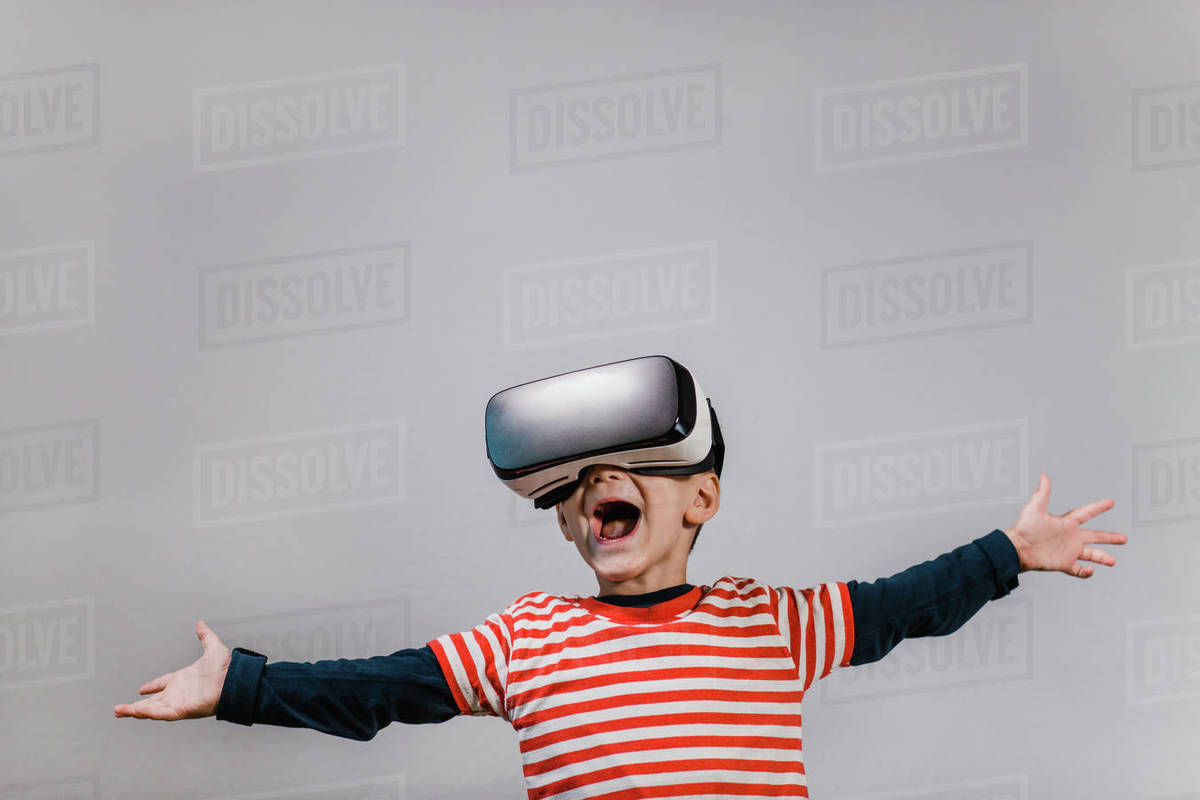 Portrait of happy child wearing virtual reality headset against grey ...