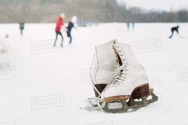 Pair of female ice skates lying on the snow with skaters in the ...