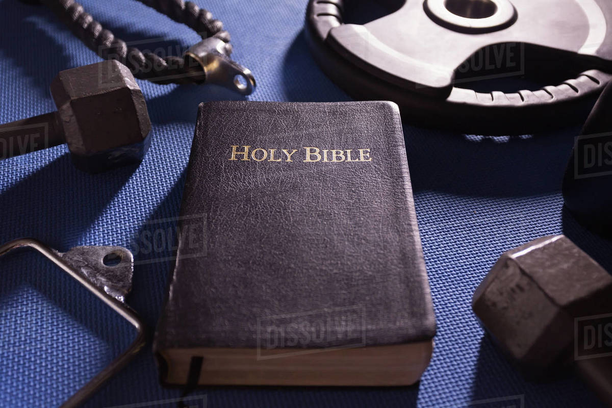 Holy Bible surrounded by dumbbells weights and other exercise equipment ...