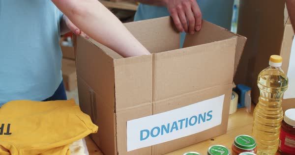 Close up of male and female food bank workers filling cardboard boxes ...