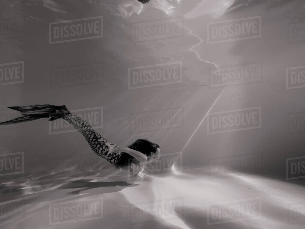 Beautiful young woman with mermaid tail swims and dives under sunlit ...