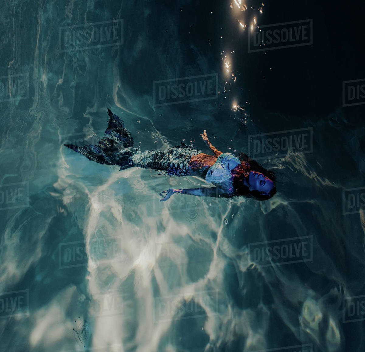 Beautiful young woman with mermaid tail swims and dives under sunlit ...