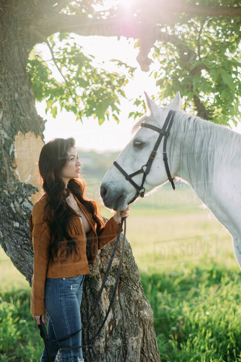 Young dreamy woman stands in unbuttoned jacket near tree and holds ...