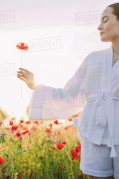 Young woman in white clothes holding poppy flower in her hand enjoying ...