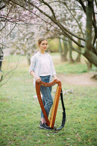 Woman harpist walks with her harp at flowering garden among blooming ...