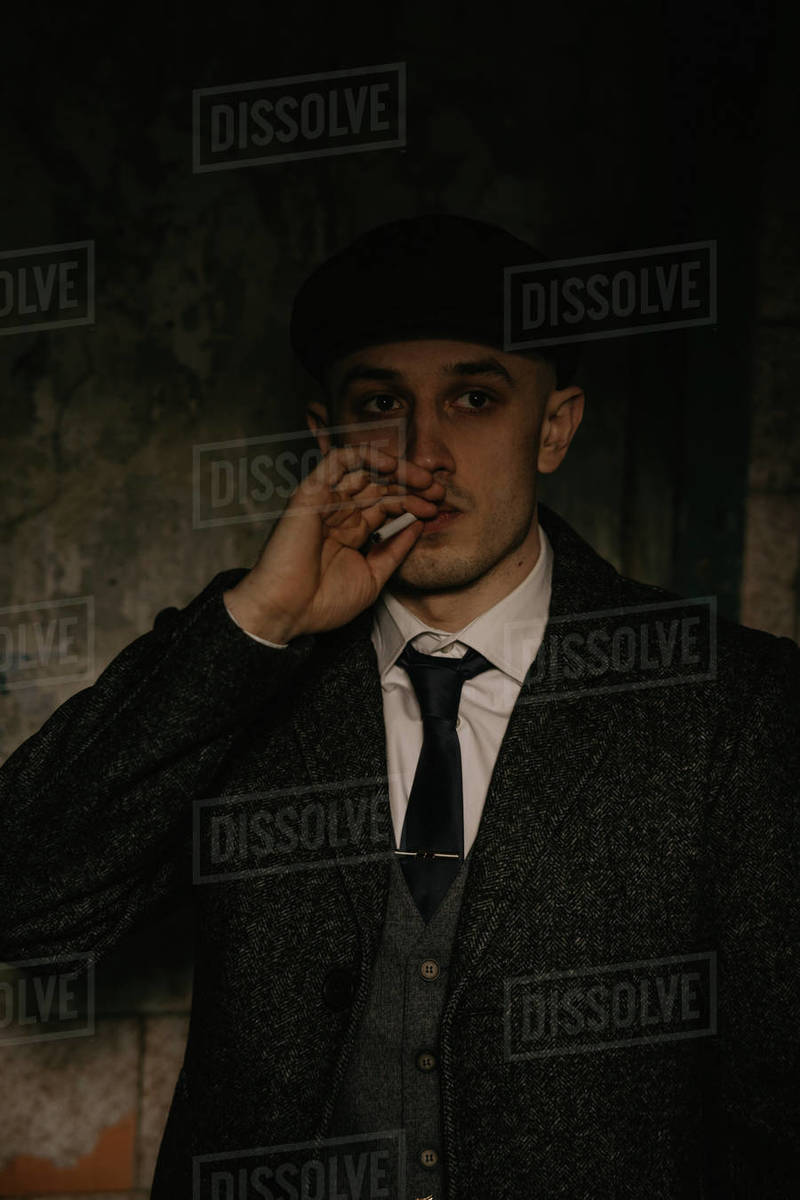 A man smokes a cigarette in the image of an English retro gangster of ...