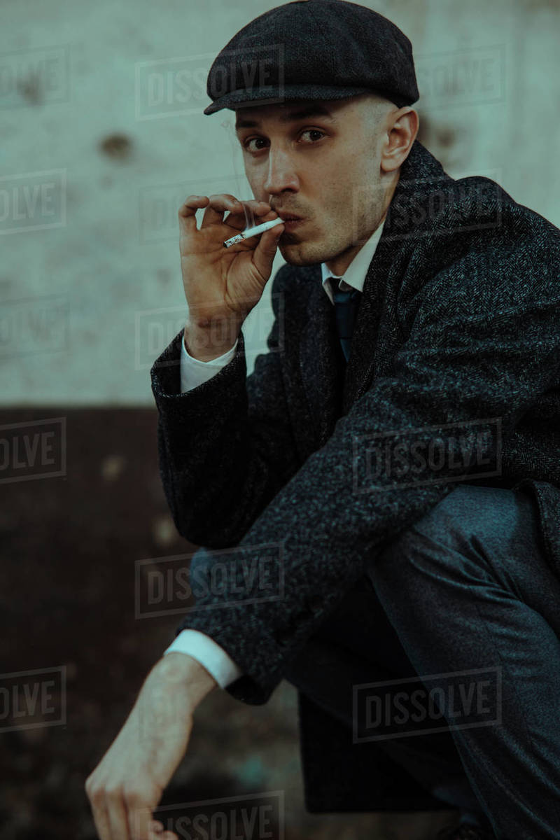 A man smokes a cigarette in the image of an English retro gangster of ...