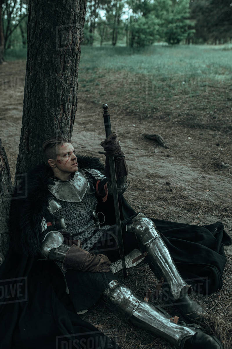 Medieval tired warrior knight in chain mail armour and black cape sits ...