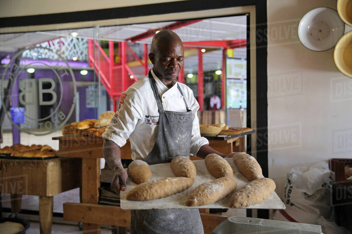 African baker carrying tray of loaves of bread in bakery - Royalty-free ...