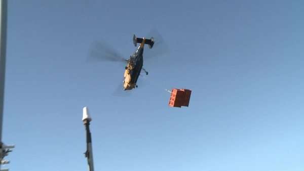 Tilting long shot of helicopter lifting container off of ship and ...