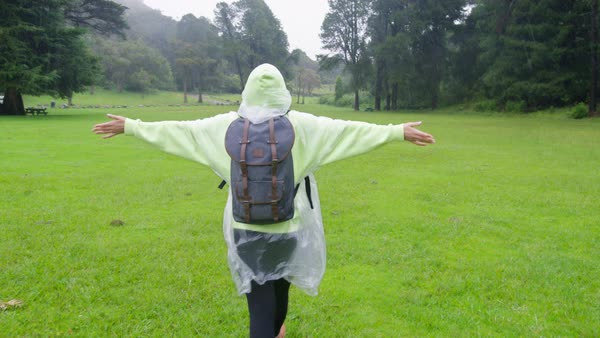 Back view happy free hiker woman with backpack, taking off hood of rain ...