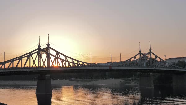 Side view of the road bridge across the river against the sun at sunset ...