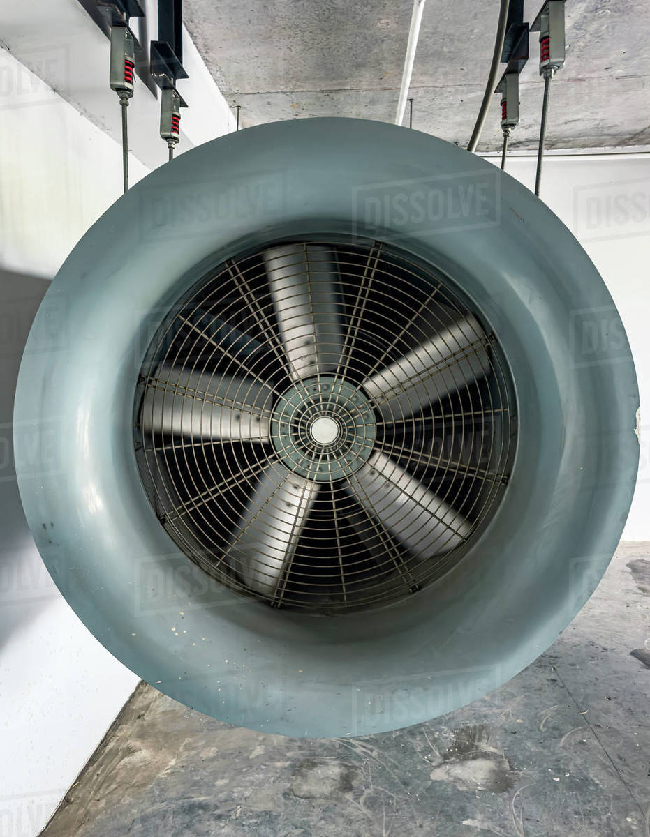 A large, gray, industrial fan is suspended from the ceiling of a ...