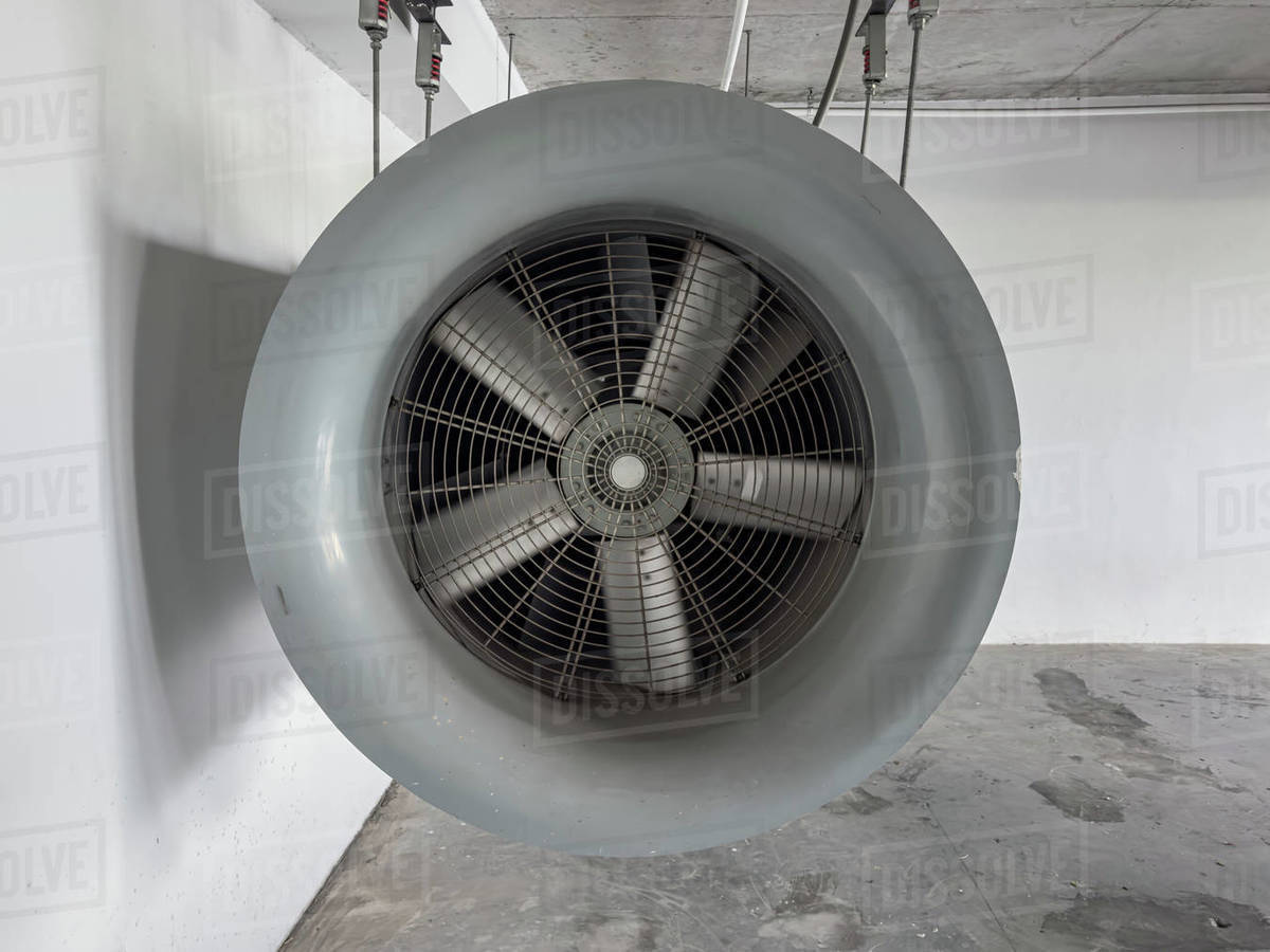 A large, gray, industrial fan is suspended from the ceiling of a ...
