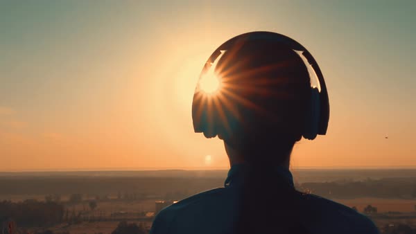 Close up back view of woman head headphones listening music at sunrise ...