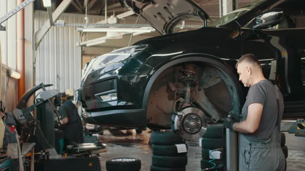Sliding shot of auto mechanic checking SUV suspension of a lifted car ...