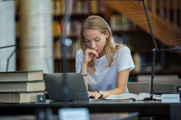 Young girl sitting at a desk in library, working at computer. Reading ...