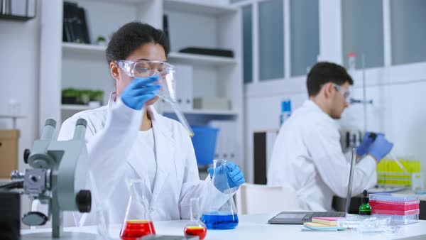 Female chemist mixing substances in lab, typing experiment report on ...